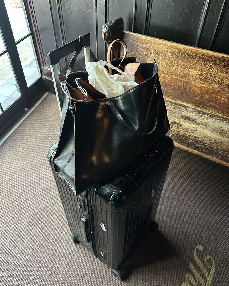 Black leather tote bag filled with travel essentials on hard shell suitcase%2C set beside wooden bench in cozy interior entryway