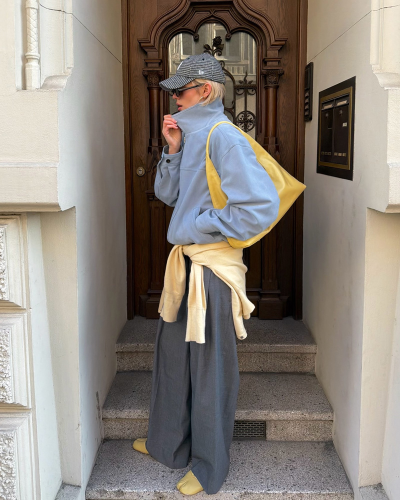 Powder blue oversized jacket with wide-leg trousers%2C styled with cap%2C yellow shoulder bag and sneakers on a townhouse entryway