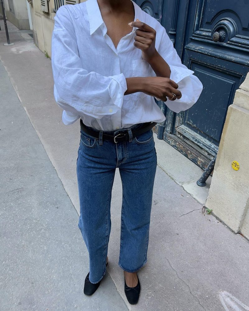 Lightweight white linen shirt paired with high-waisted blue wide-leg jeans and chic black mules%2C set against a charming Parisian backdrop