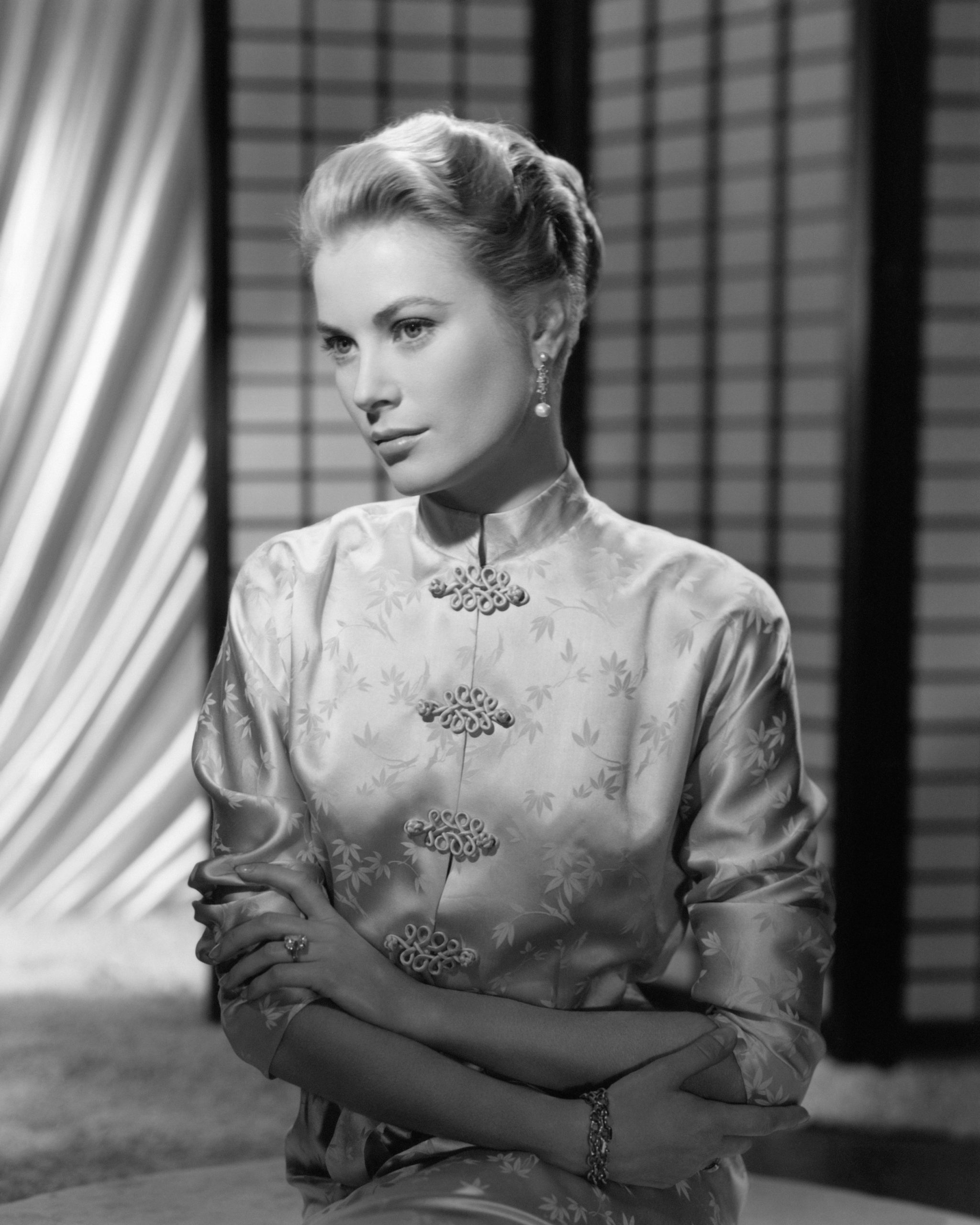 Grace Kelly wearing a vintage silk cheongsam dress with floral patterns and traditional frog closures%2C styled with pearl drop earrings and a delicate bracelet
