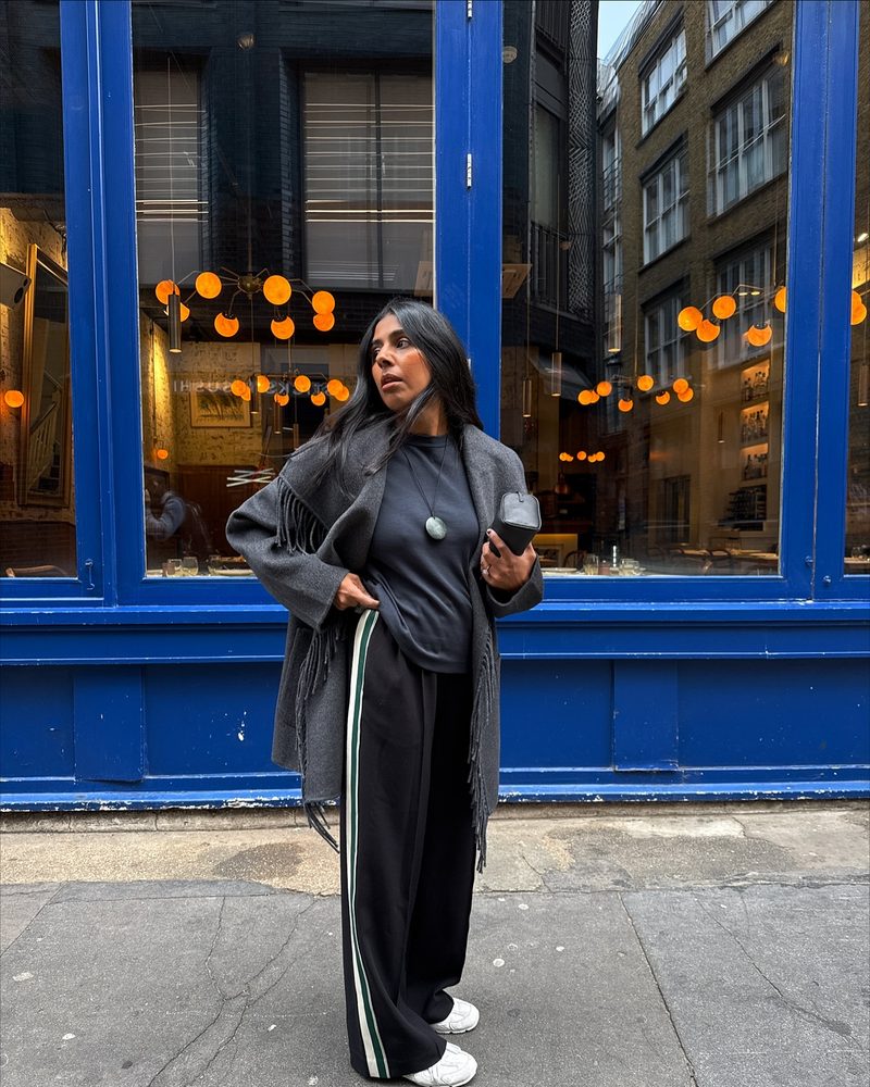 Monikh styles black track pants with green side stripes%2C a relaxed gray top%2C and a fringed gray coat for a chic urban look.