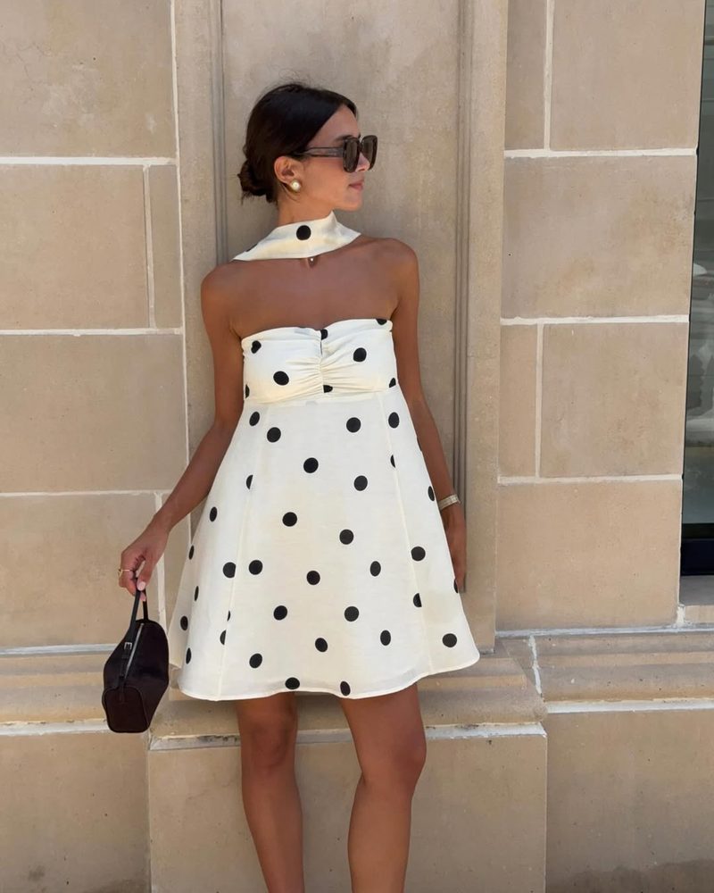 White polka dot strapless mini dress with neck scarf detail%2C styled with sunglasses and brown mini bag for chic summer outfit