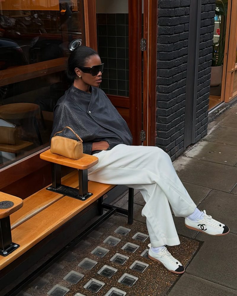 Black leather jacket with white trousers and Chanel sneakers%2C styled with sunglasses and mini bag for effortless street style