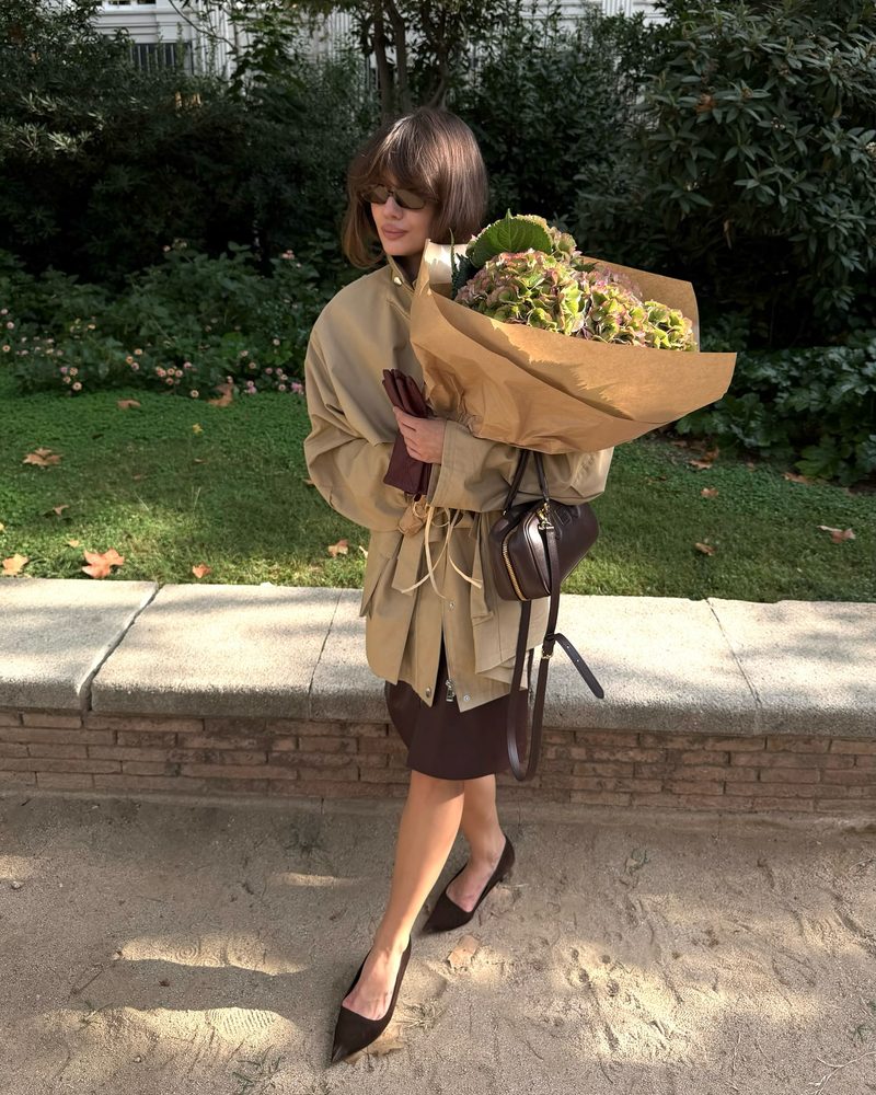 Chic autumn outfit featuring a light beige oversized jacket%2C a dark brown skirt%2C and sleek pointed-toe heels%2C complemented by a stylish handbag and fresh bouquet