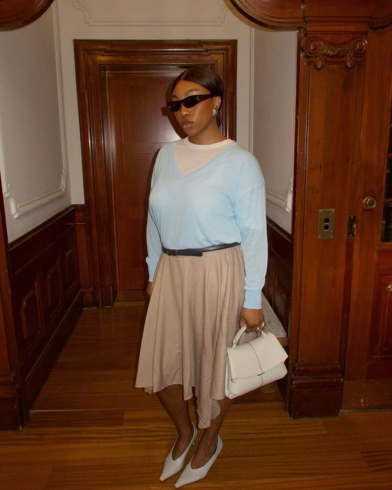 Pastel outfit with light blue sweater layered over white tee and beige asymmetrical skirt%2C styled with white heels and mini top handle bag