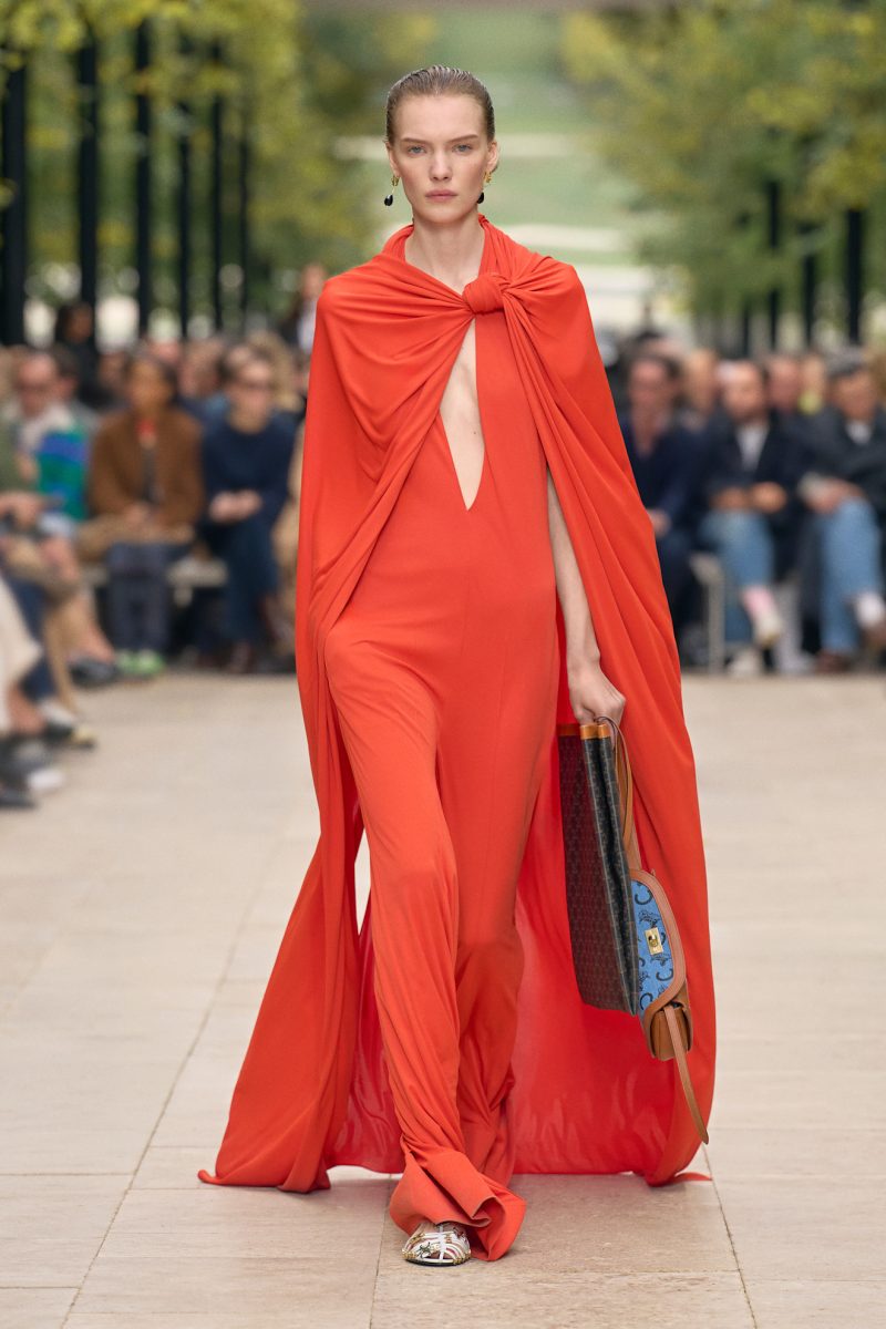 Celine spring 2026 orange flowing gown with cape detail, deep neckline, and structured handbag on runway