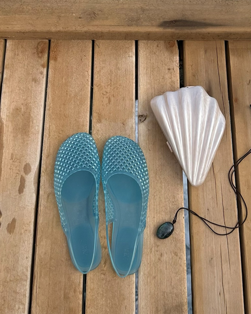 Blue rubber ballet flats with textured finish%2C paired with a white shell clutch and pendant necklace on wooden deck backdrop