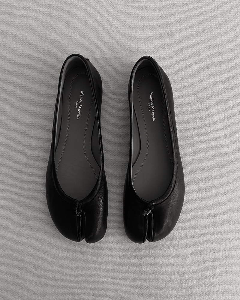 Maison Margiela black leather tabi ballet flats with split toe design on gray textured background
