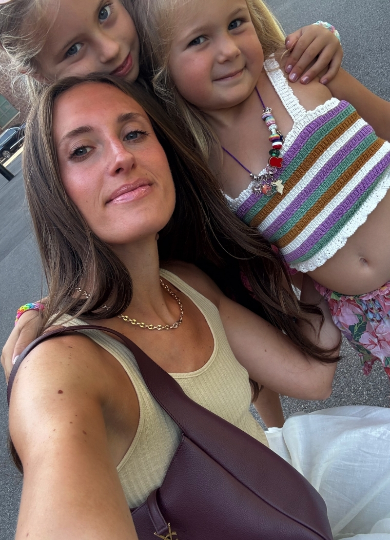 Mother with two daughters in casual summer outfits, wearing ribbed tank and striped knit top, posing outdoors on sunny street