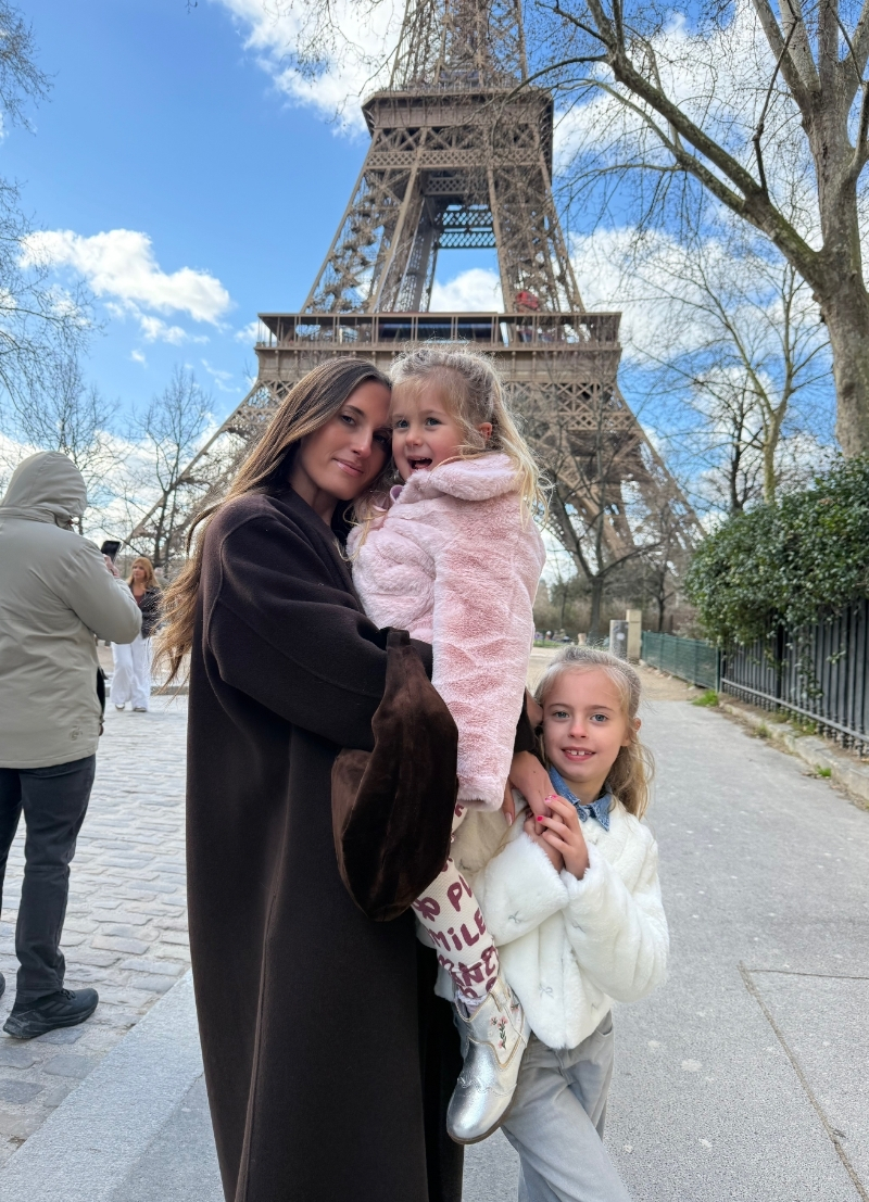 Mother with children in cozy coats, wearing long dark overcoat and pastel jackets, posing near Eiffel Tower on Paris street