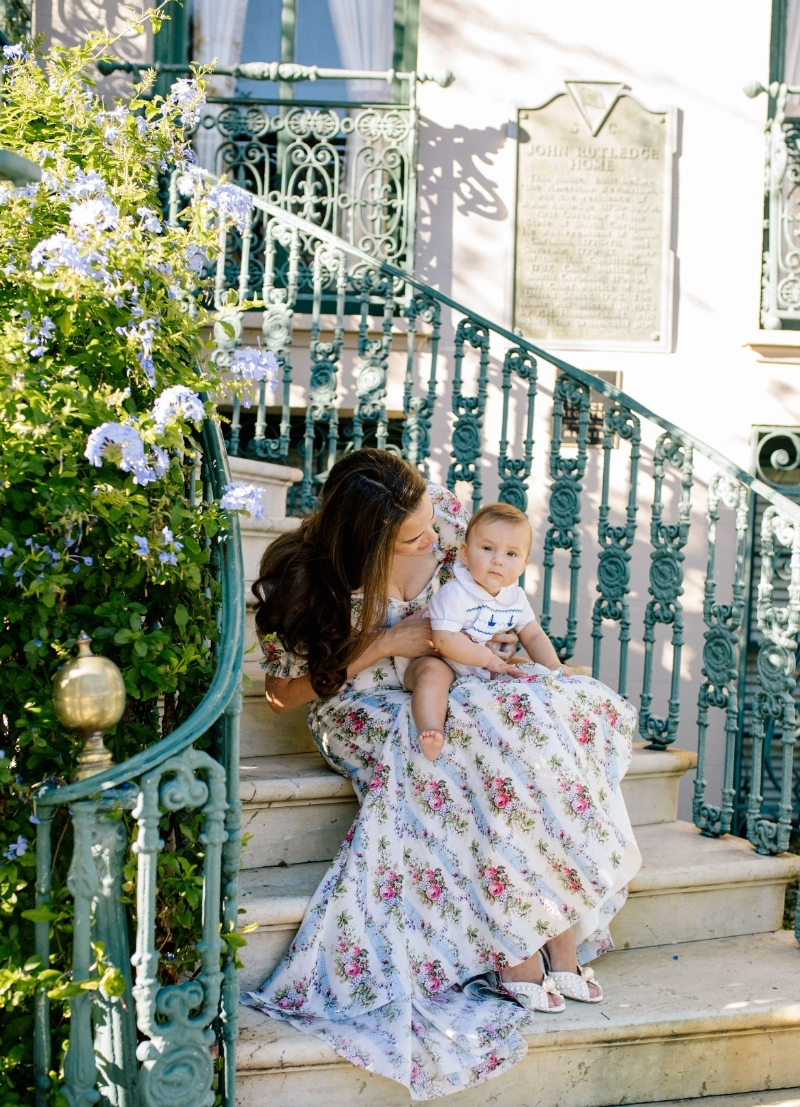Mother holding baby in floral maxi dress with puff sleeves, styled on sunlit garden staircase with wrought iron railing