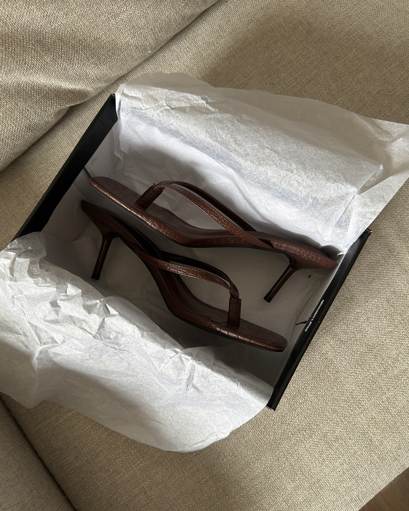 Brown leather heeled flip-flop sandals with slim straps and stiletto heel%2C displayed in tissue-lined box on neutral fabric surface