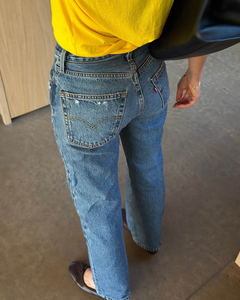 Close-up of straight-leg blue denim jeans styled with yellow tee and black shoulder bag%2C casual look on polished concrete floor
