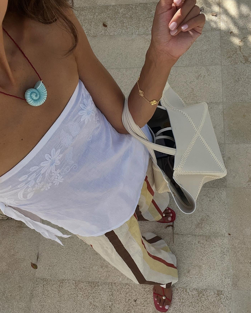 White strapless top with striped skirt%2C shell pendant necklace%2C sandals and structured tote styled on sunlit stone pavement