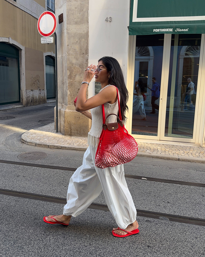 Summer street style with crochet sleeveless top and white wide-leg pants%2C styled with red net tote and flip-flops on city street
