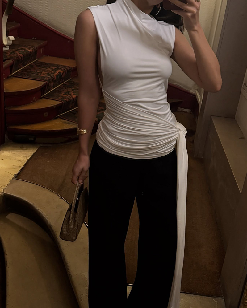 Chic evening outfit with ruched white sleeveless top and black trousers%2C styled with mini clutch in warm-toned stairway setting