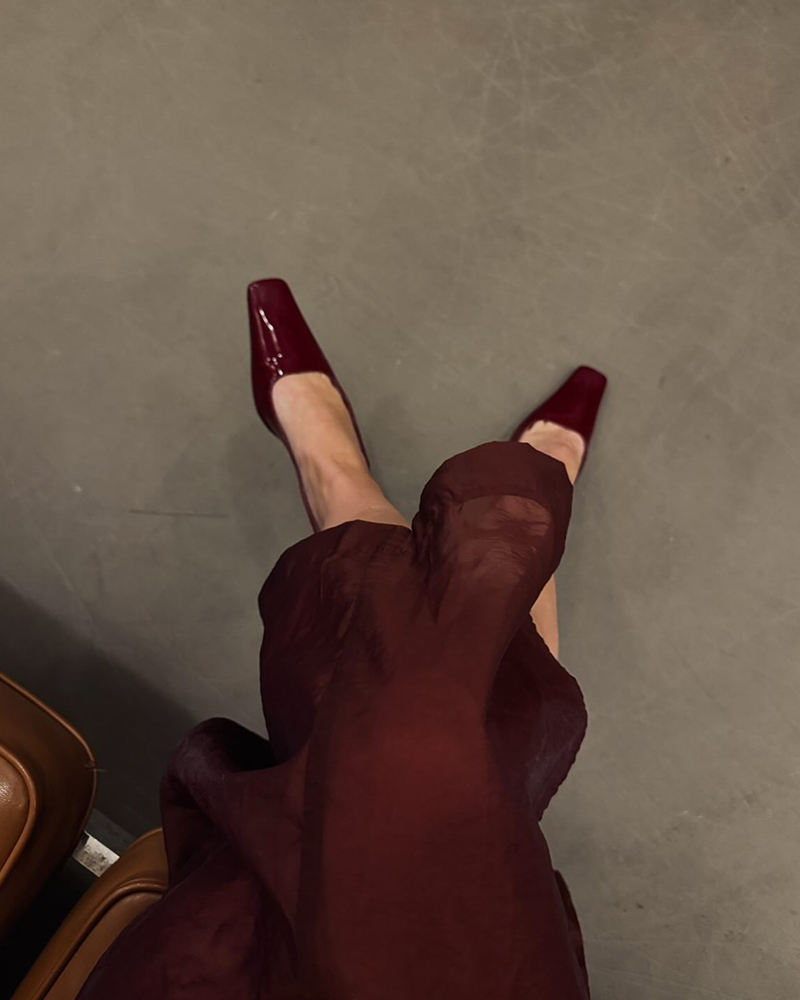 Burgundy sheer skirt with matching patent leather pumps styled from above on neutral floor in minimalist indoor setting