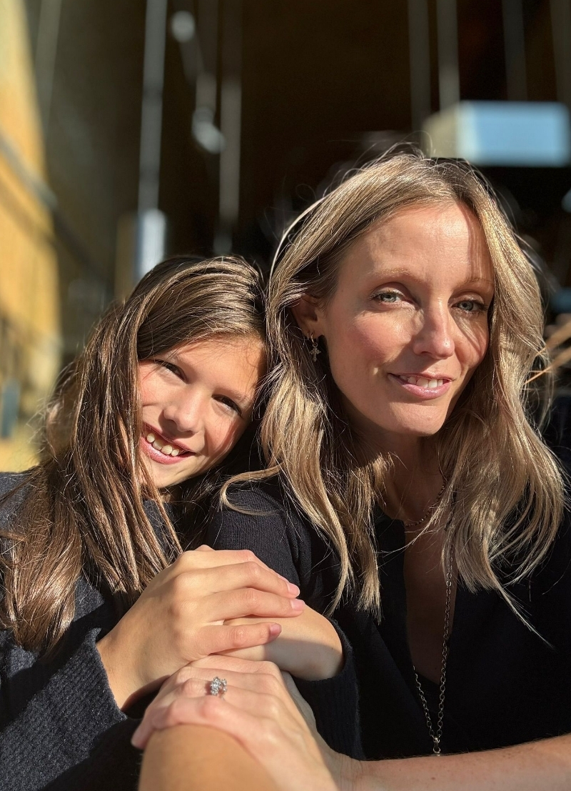 Close-up of mother in black top with gold jewelry embracing child, styled in warm natural light