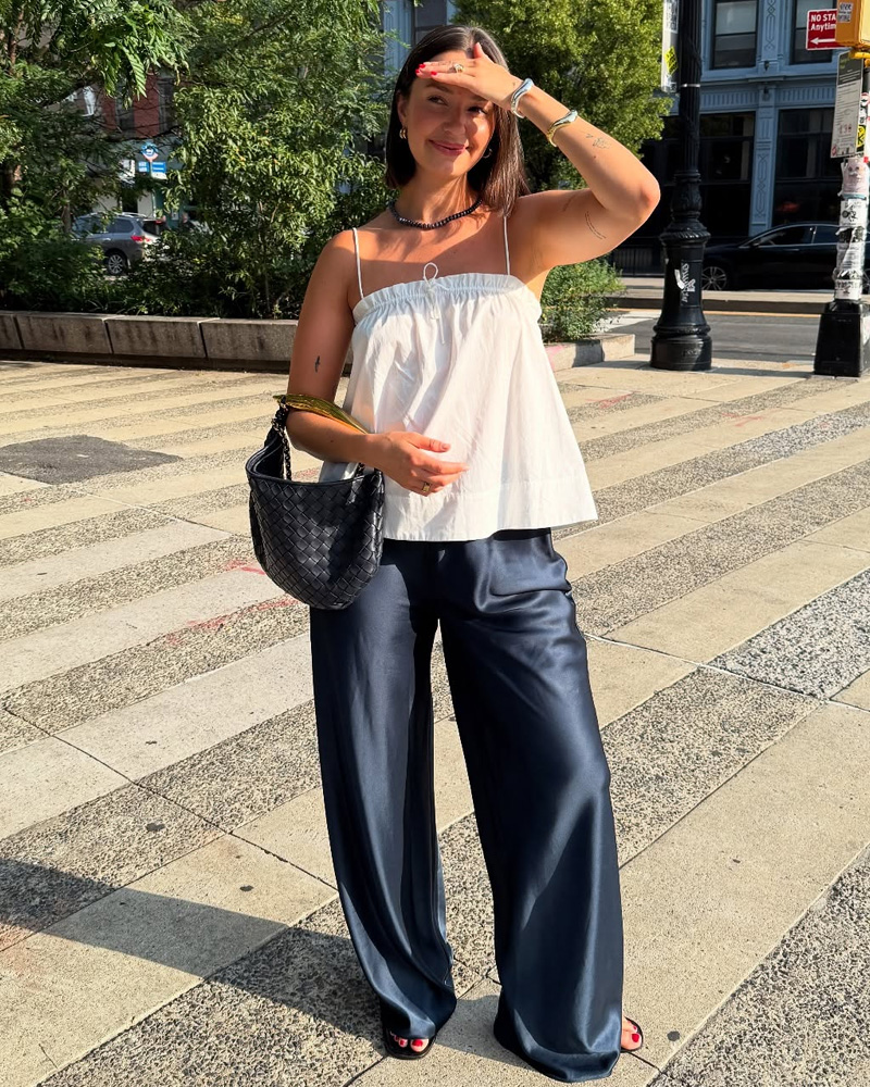 Woman in white cotton poplin camisole with navy satin wide-leg pants and woven leather bag%2C styled on a sunny city street