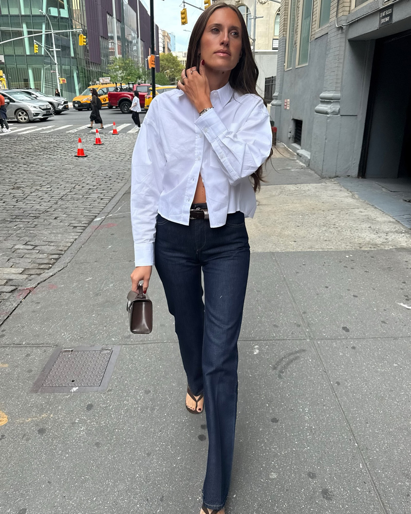 Woman in crisp white button-down shirt and dark indigo straight-leg jeans with mini leather bag%2C walking on a city street