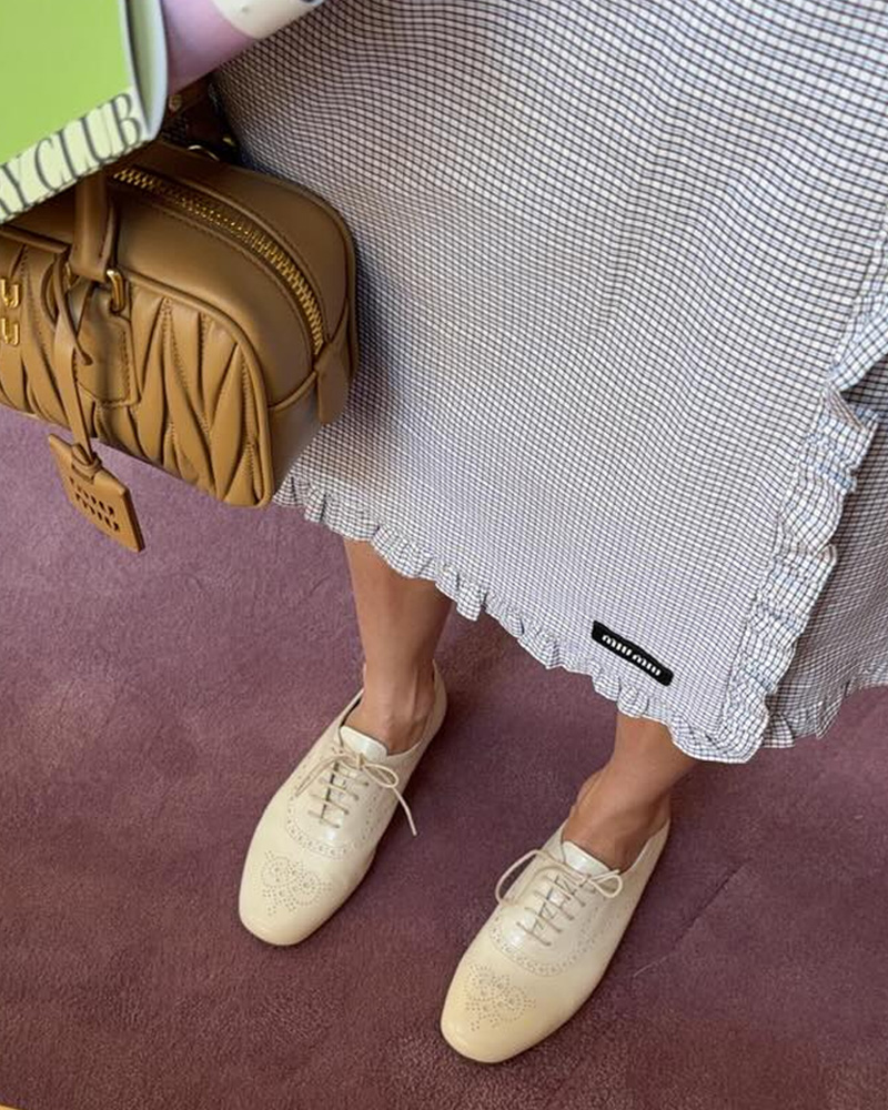 Cream lace-up leather oxford shoes styled with gingham midi skirt and tan mini bag on soft pink carpet backdrop