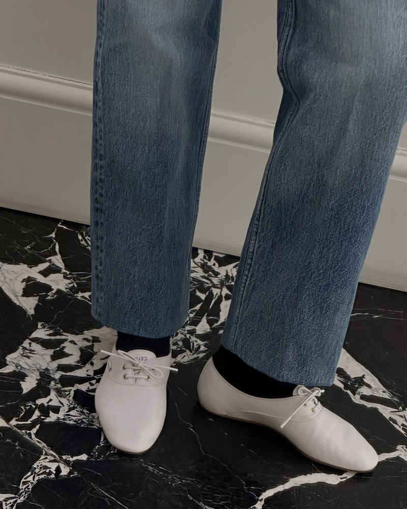 White leather derby shoes styled with straight-leg blue jeans and black socks%2C set against a polished marble floor backdrop