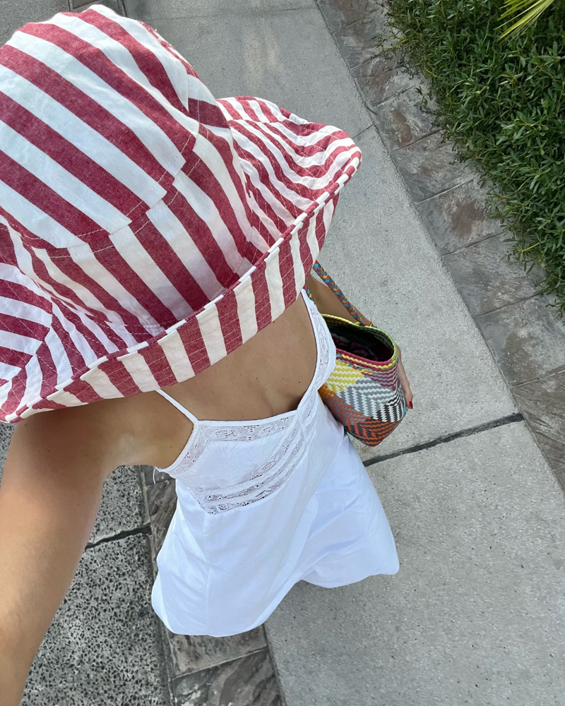 White lace sundress styled with a red striped sun hat and colorful woven tote for a chic summer vacation outfit
