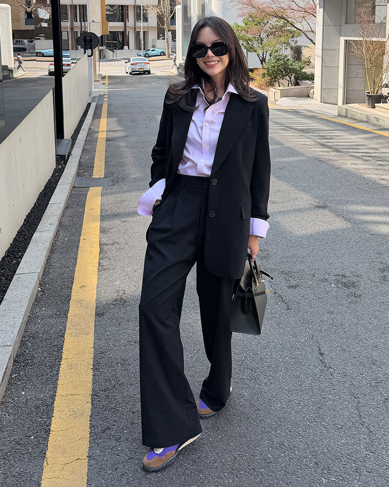 Woman in black tailored suit with pink button-down shirt%2C sunglasses and leather handbag%2C styled on city street in daylight