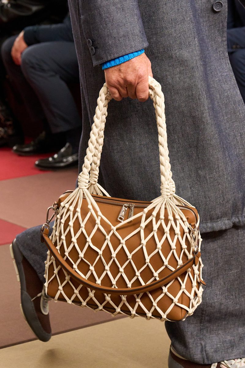 Tan leather top-handle bag with cream braided net overlay and shoulder strap paired with a tailored gray suit look