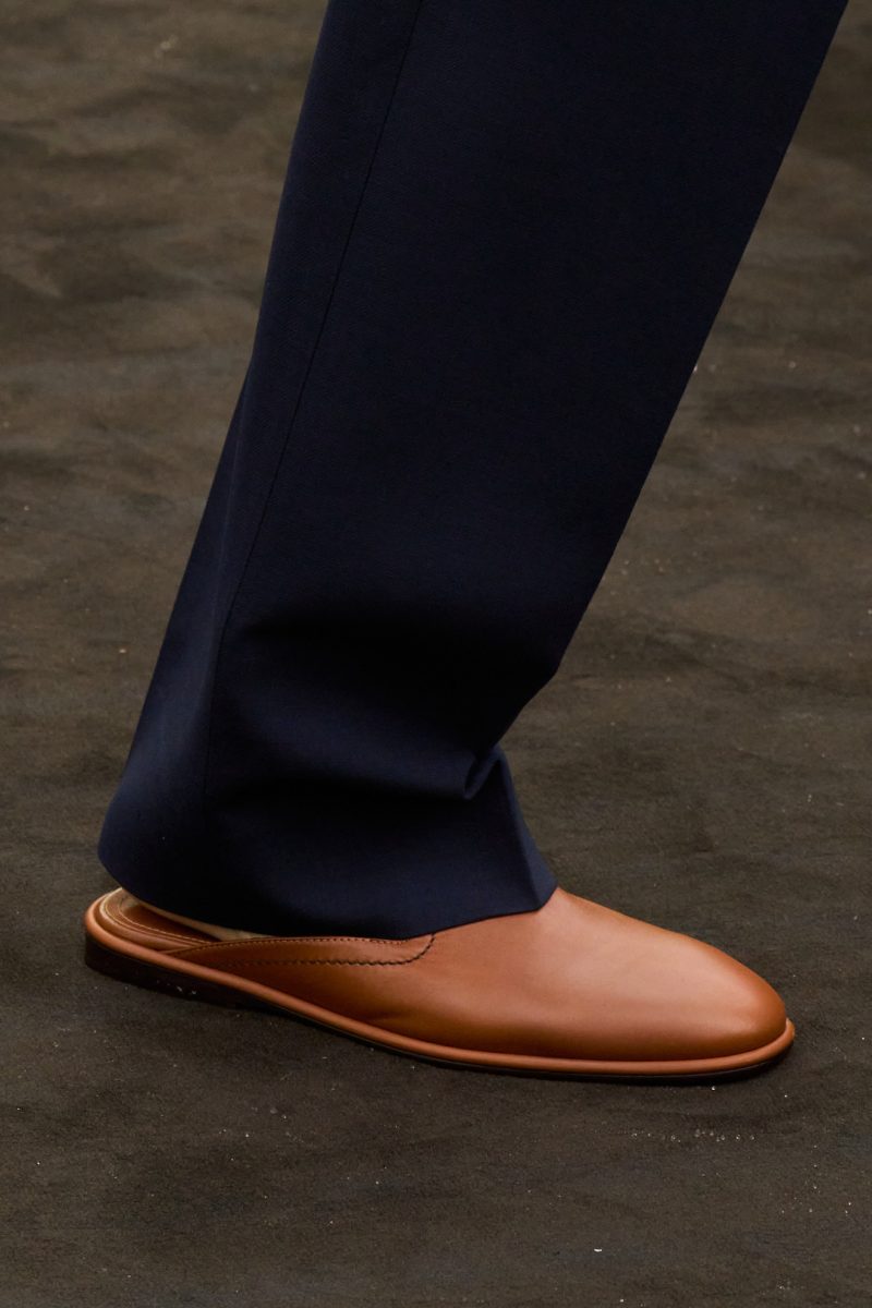 Brown leather slip-on mule from Ferragamo paired with tailored navy trousers on runway floor