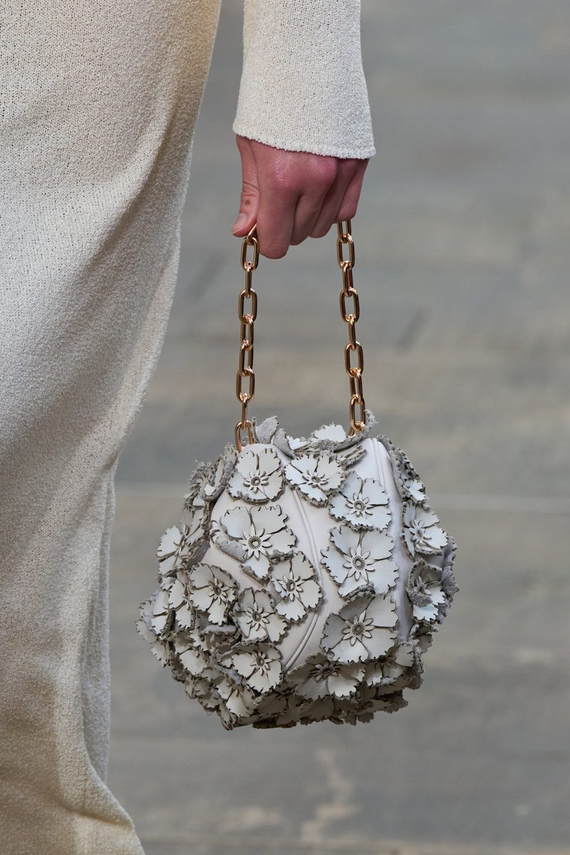 White floral appliqué mini handbag with gold chain handle, paired with a textured ivory dress for an elegant runway look
