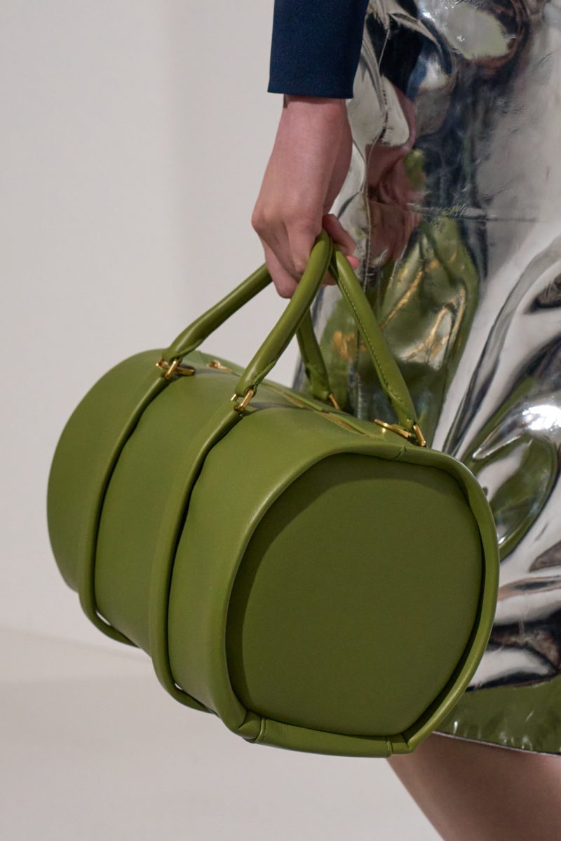 Olive green leather mini top handle bag with sculptural cylindrical panels, styled with metallic skirt for modern runway look