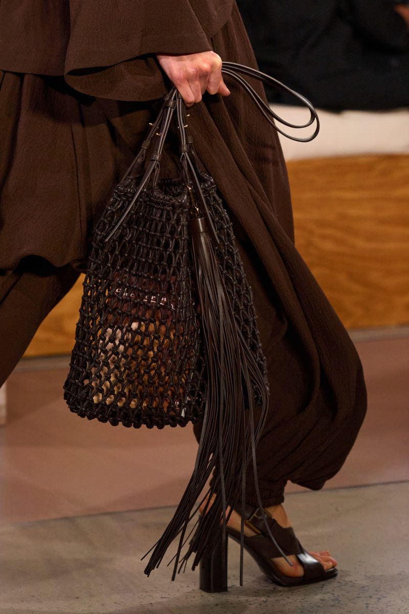 Dark brown woven net bucket bag with long leather tassels paired with a flowing brown dress and heeled sandals