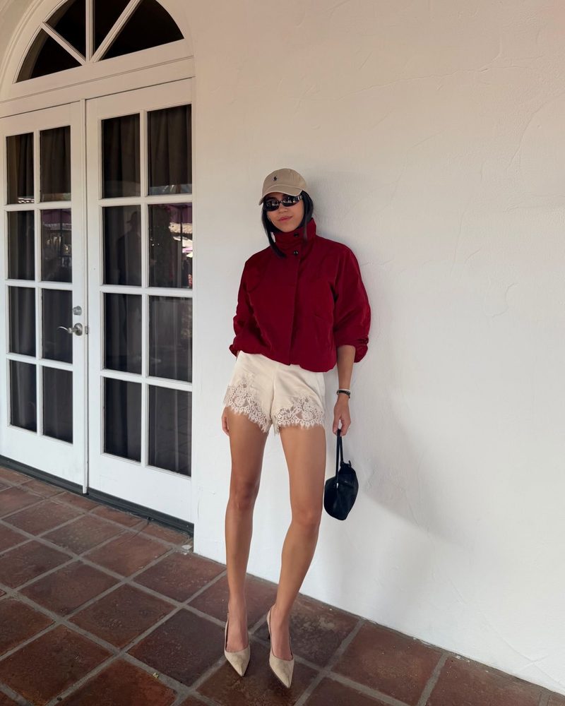 Sophisticated look featuring a red cropped jacket%2C cream lace-embellished shorts%2C and beige pointed-toe heels%2C paired with a baseball cap and chic sunglasses