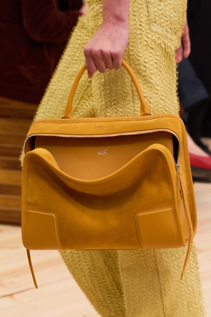Loewe mustard yellow suede top handle bag with sculptural curved front pocket, styled with textured yellow dress on runway