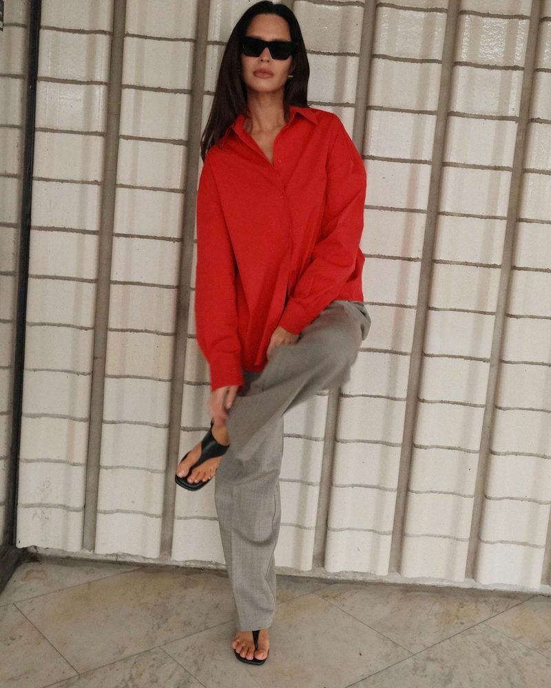 Chic minimalist outfit featuring an oversized red button-up shirt paired with tailored gray trousers and sleek black sandals%2C perfect for warm weather styling