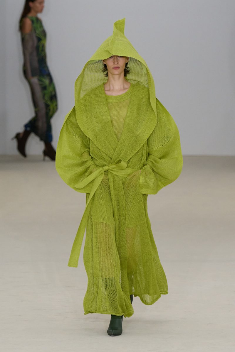 Model wearing a lime green oversized knit coat with a large hood and belt from Issey Miyake spring summer 2026 collection