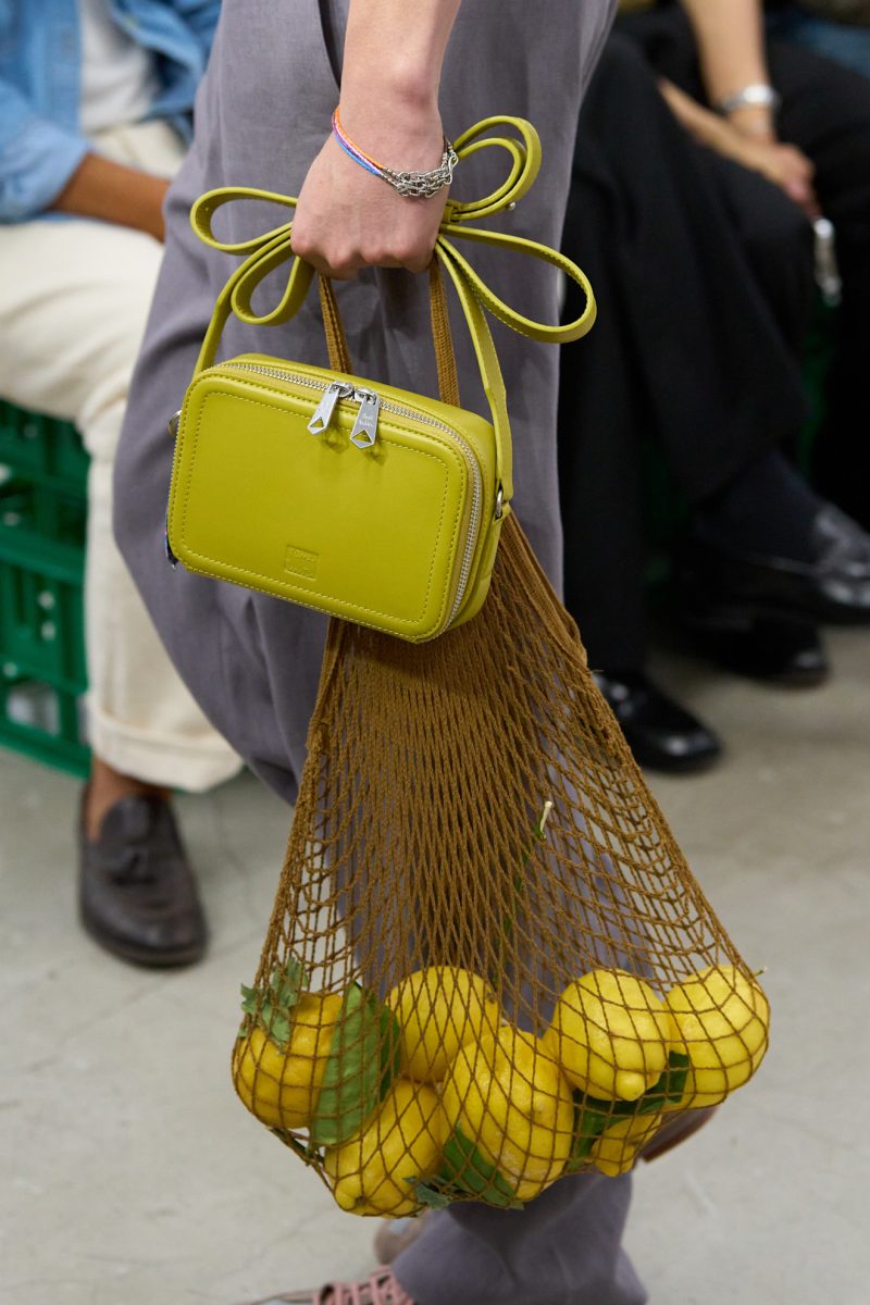 Chartreuse leather mini crossbody bag with double zip and bow detail, paired with mesh tote filled with lemons for market style