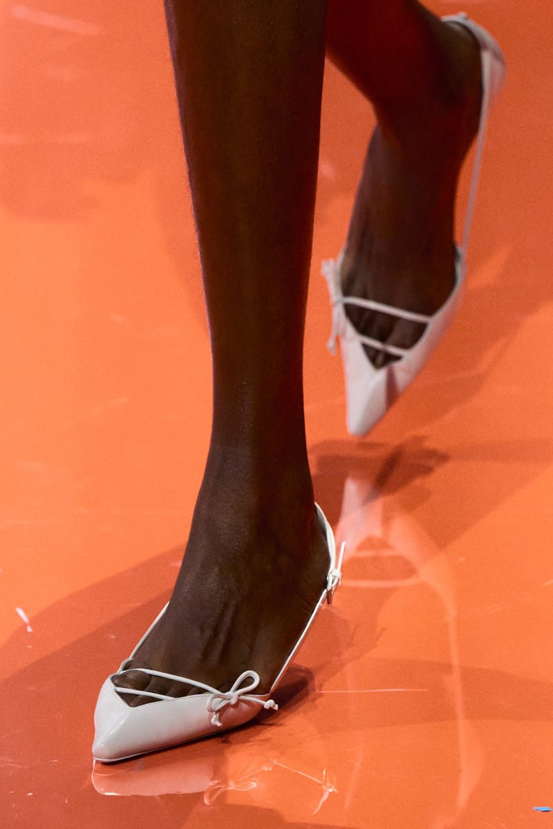 Prada white pointed slingback flats with delicate bow and thin strap detail on glossy orange runway floor