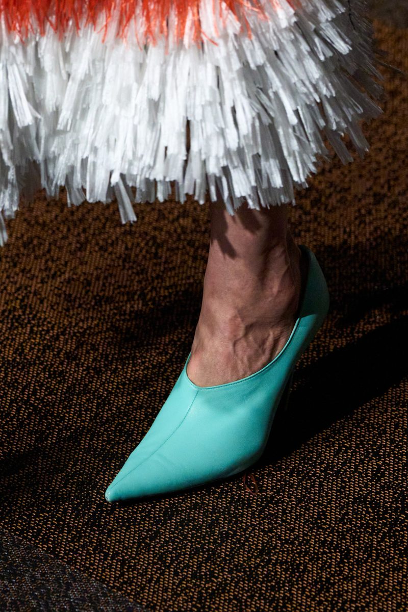 Turquoise leather pointed-toe flat shoe paired with a white and orange fringed skirt on runway