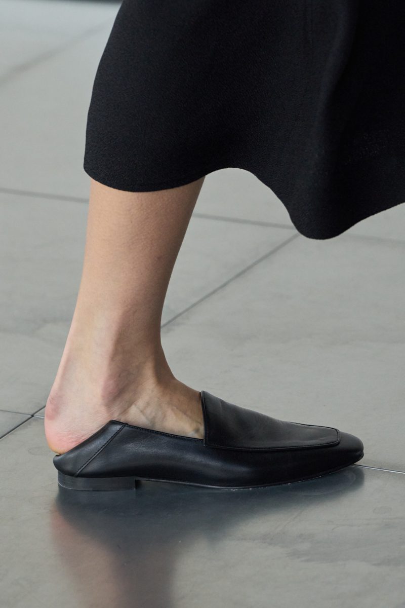 black leather slip-on mule with square toe paired with a black midi skirt on a tiled floor