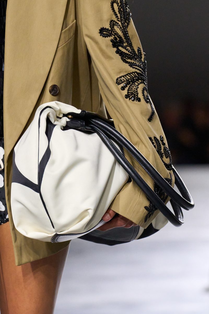 Two-tone leather top handle bag in cream and black paired with embroidered beige blazer, highlighting soft folds and structured handles for runway style