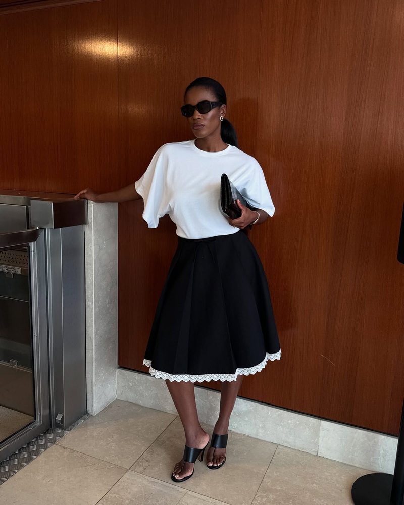 Chic summer outfit featuring a relaxed white oversized t-shirt paired with a black pleated skirt accented by lace%2C accessorized with sleek sunglasses and a clutch