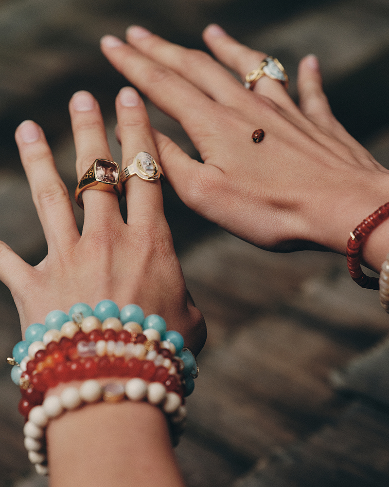 Close-up of stacked beaded bracelets and gemstone rings on hands against a natural backdrop