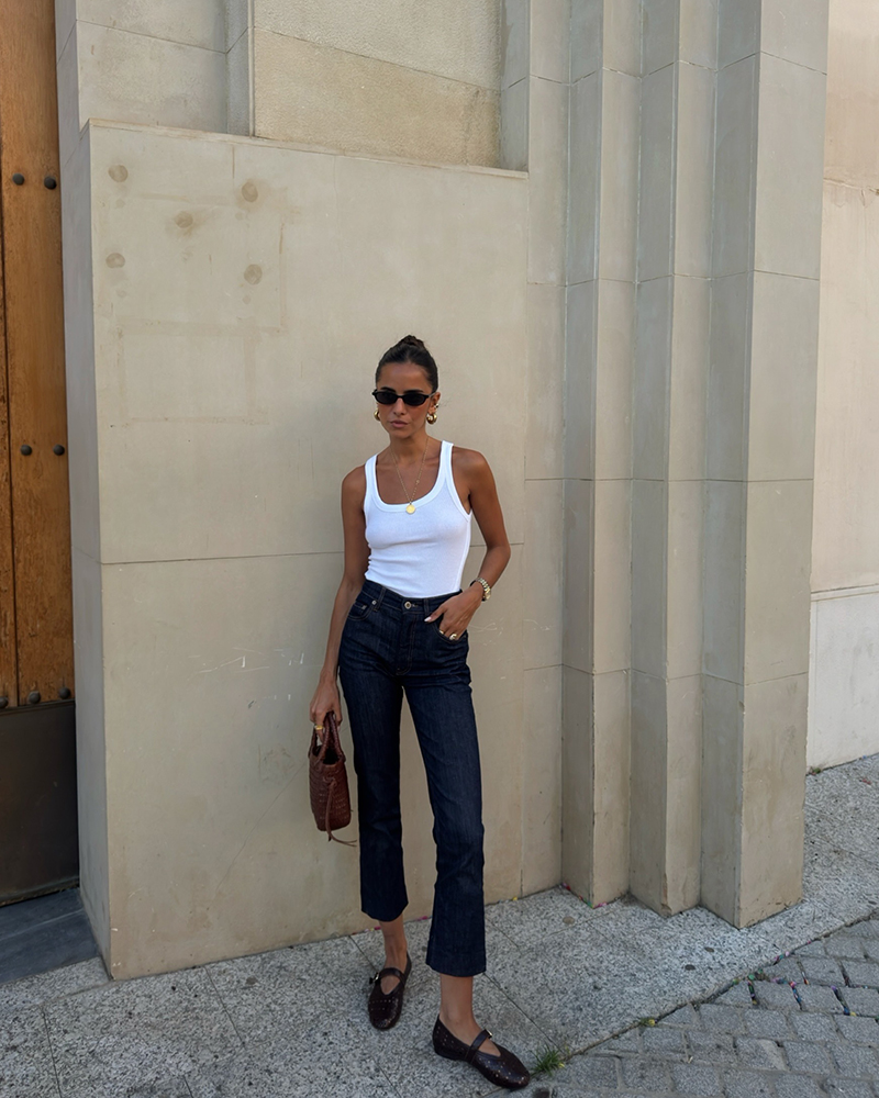 White ribbed tank top with cropped dark denim jeans and brown woven flats styled on a city sidewalk