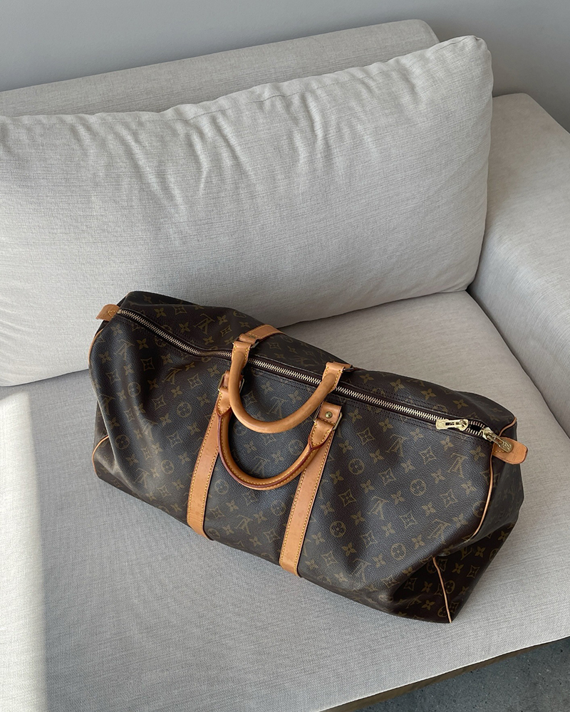 Louis Vuitton Keepall duffle bag in monogram canvas with tan leather handles%2C styled on a cream sofa