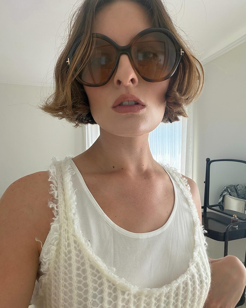 Oversized brown sunglasses styled with a white textured knit tank in a softly lit minimalist interior