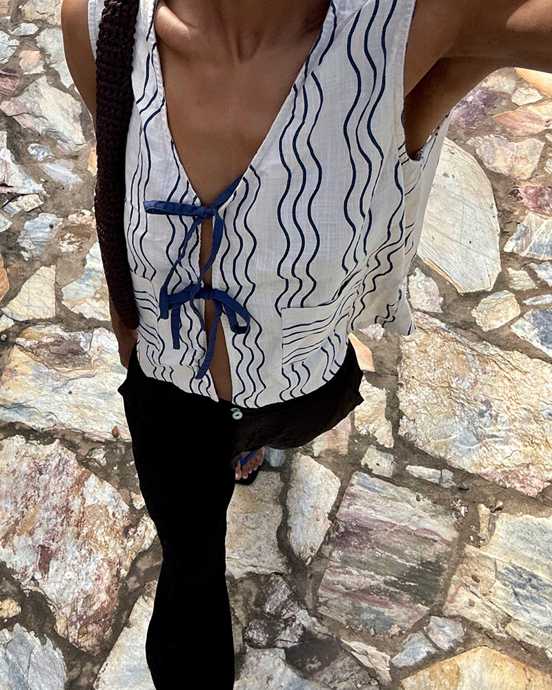 White linen tie-front top with navy wave print paired with black trousers on a sunlit stone terrace in summer