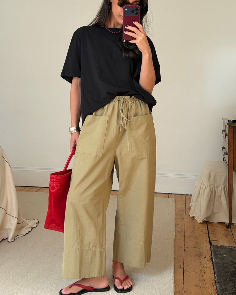 Black oversized tee with khaki wide-leg drawstring pants and red sandals styled in a minimalist home setting