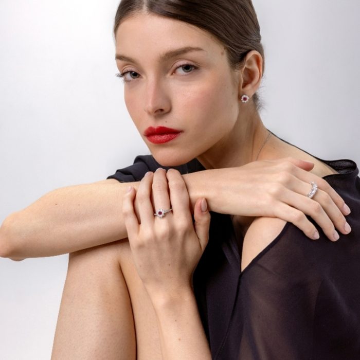 Model in sheer black dress styled with diamond bracelet, ruby ring and stud earrings against soft gray backdrop